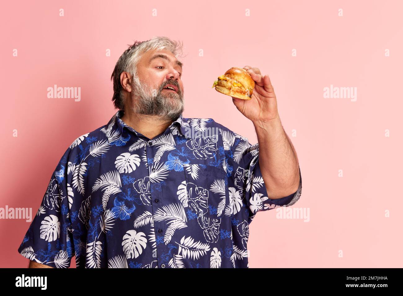 Portrait of mature man in colorful shirt posing with delicious burger ...