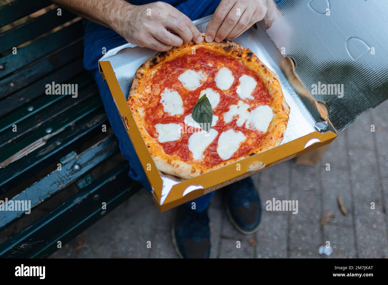 Relaxed Enjoyment: Man savoring Neapolitan pizza on a park bench from a ...