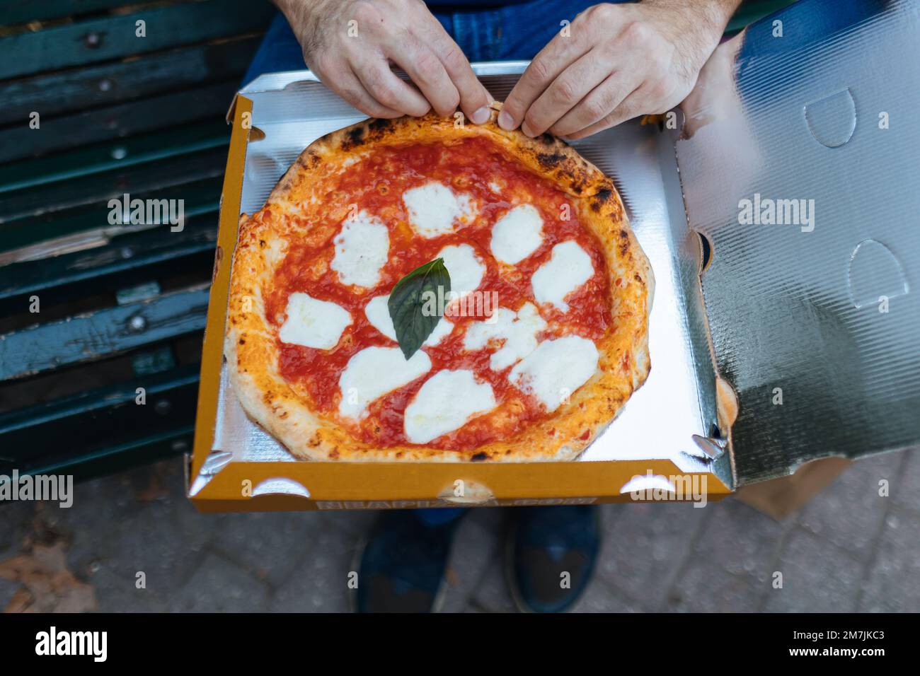 Relaxed Enjoyment: Man savoring Neapolitan pizza on a park bench from a ...