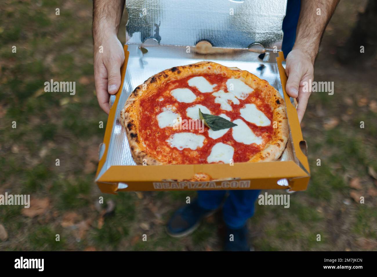Relaxed Enjoyment: Man savoring Neapolitan pizza on a park bench from a ...