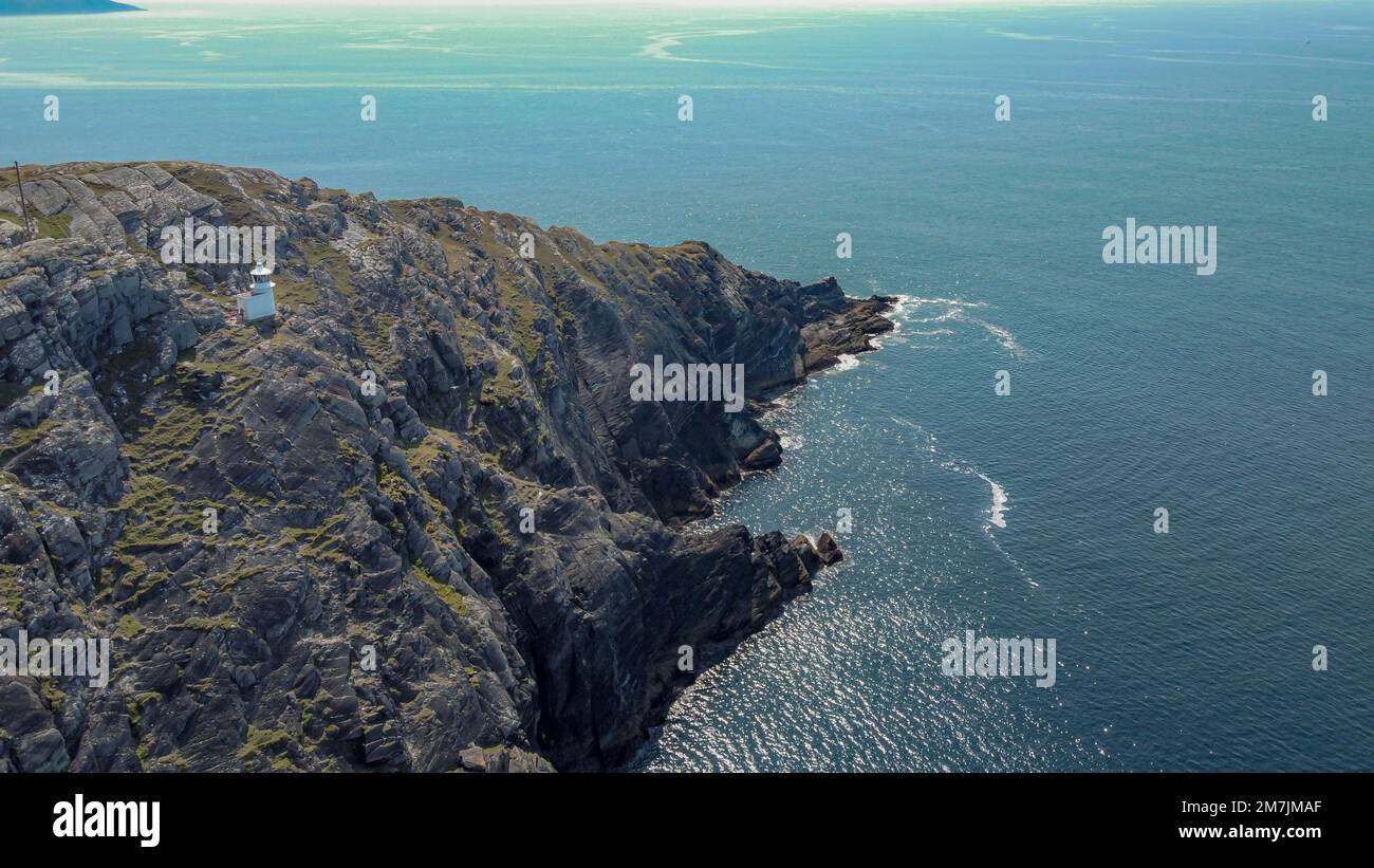 A bird's-eye view of a lighthouse on rough rocky cliffs by the sea ...