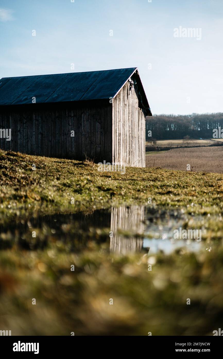 A vertical shot of an old wooden barn and its reflection on a puddle ...