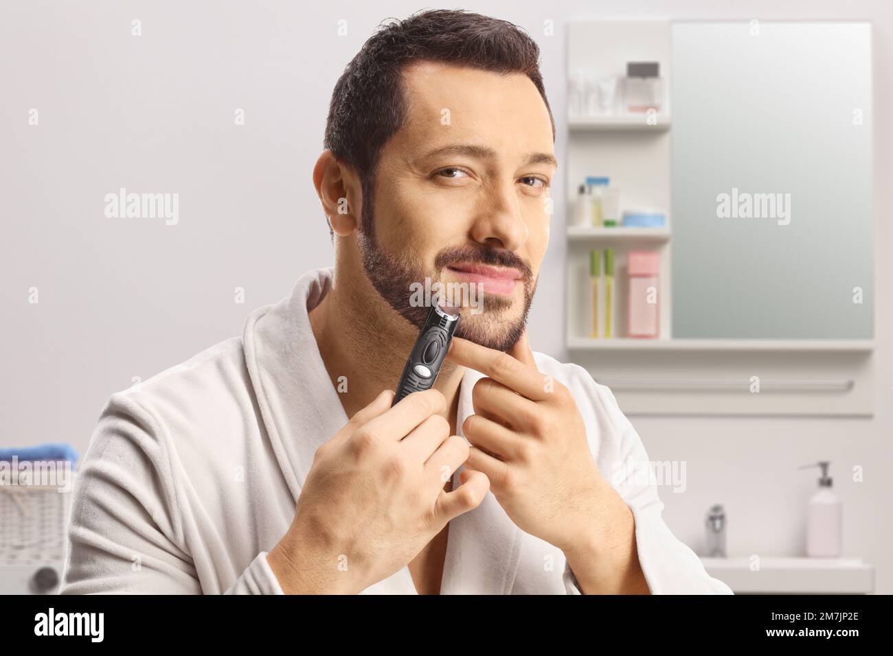 Young man in a bathrobe using a beard trimmer inside bathroom Stock Photo - Alamy