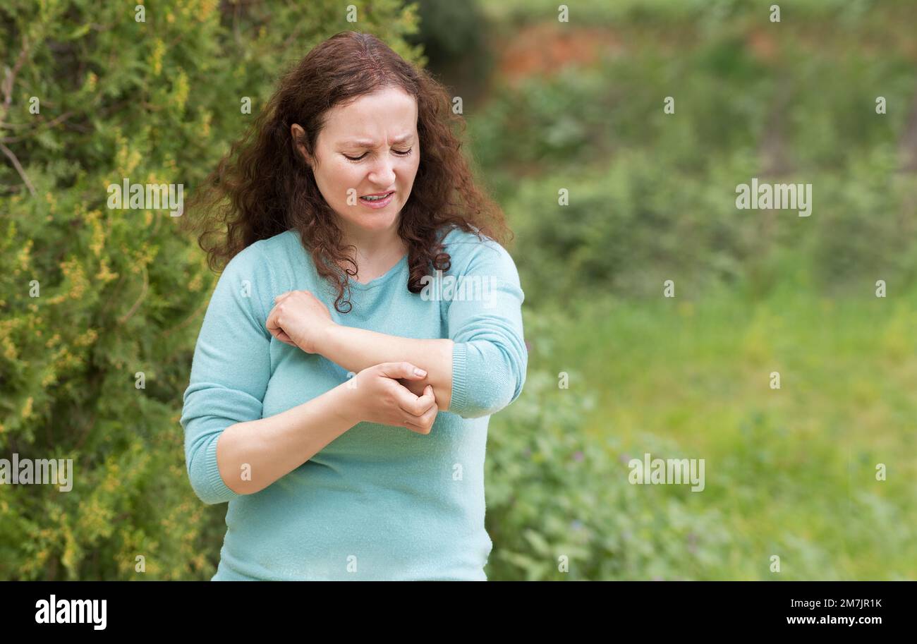 Woman scratching arm because it stings in a park with copy space Stock ...