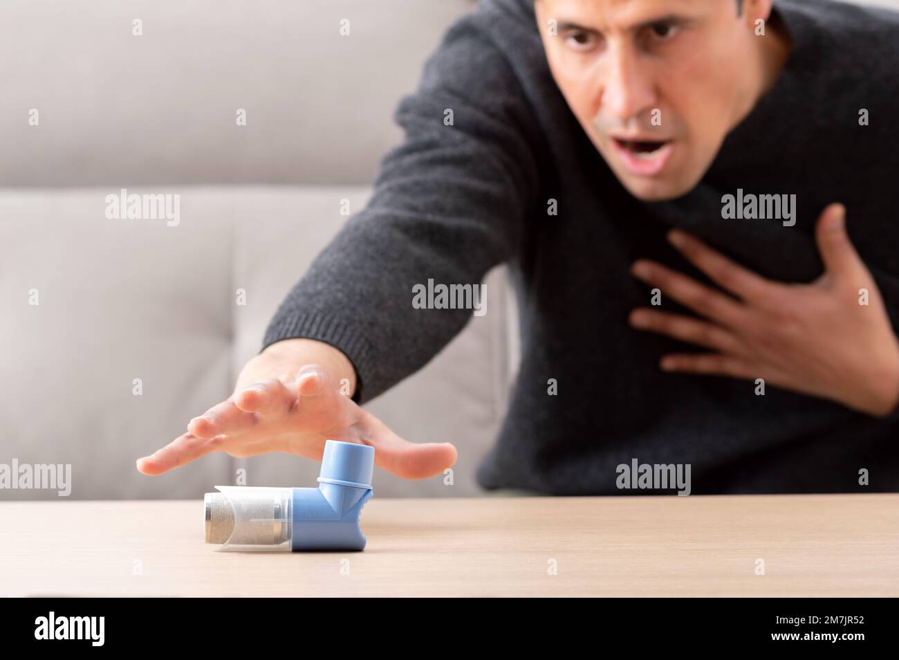 Man suffering asthma attack reaching inhaler sitting on a couch in the ...