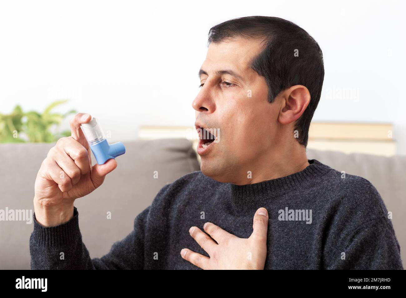 Man holding inhaler with asthma attack suffocating sitting on a couch ...