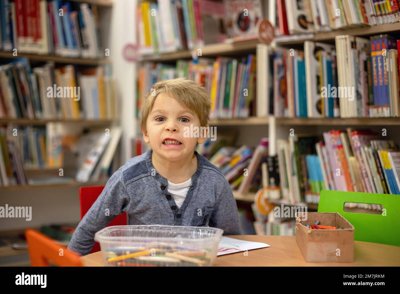 Adorable little child, boy, sitting in library, reading book and ...