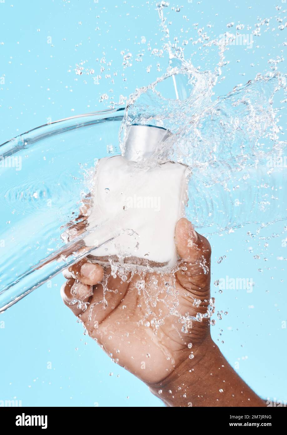 Water splash, black man and hand with skincare bottle in studio on a blue background. Hygiene ...