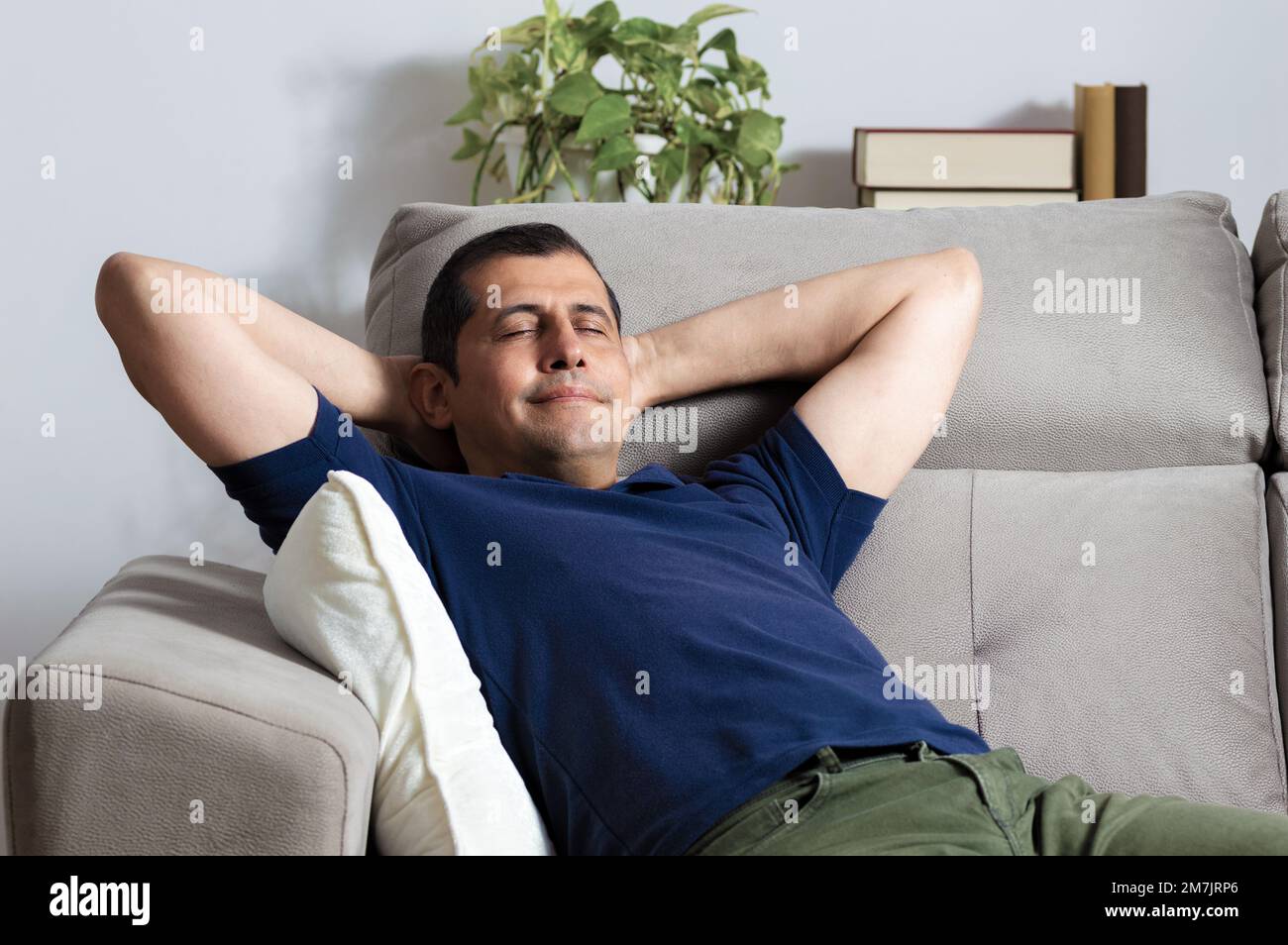 Happy man relaxing with arms on head sitting on a couch in the night at ...