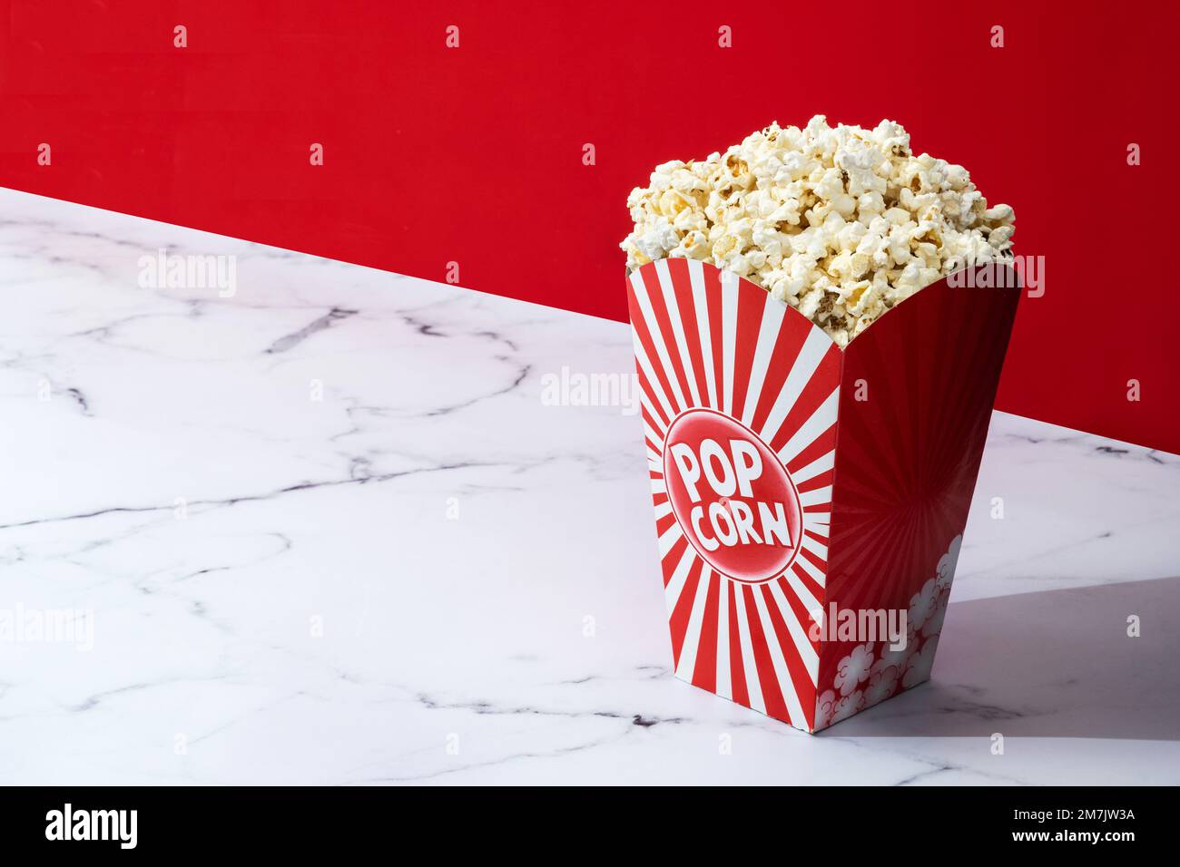 Salted popcorn in carton package on white marble and red background ...
