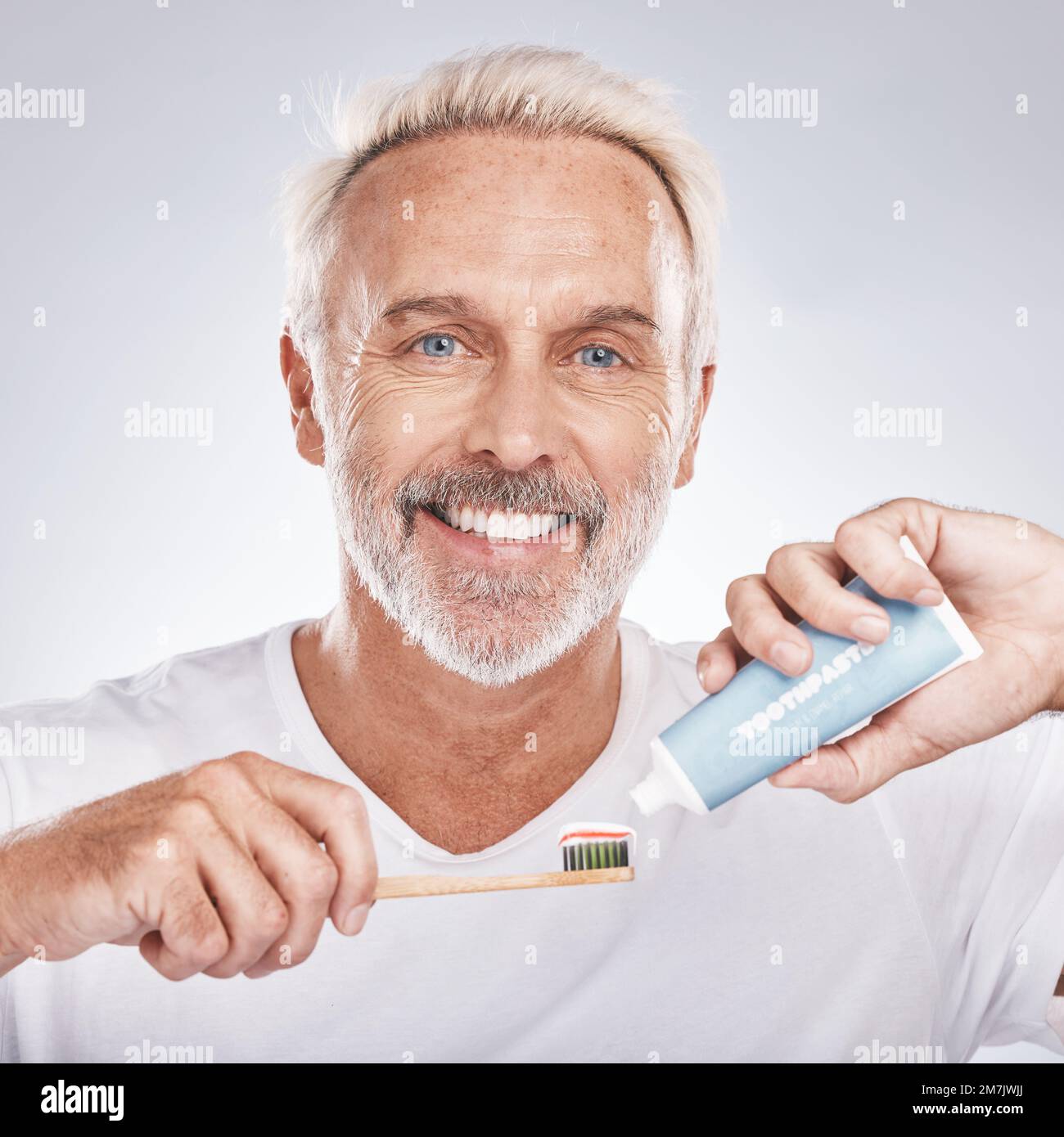 Toothbrush, face and senior man with toothpaste in studio on a gray ...
