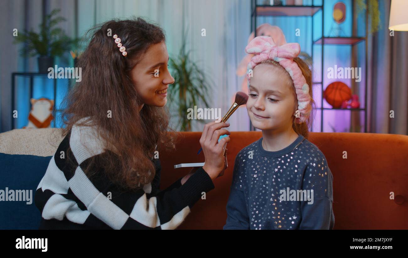 Teenage child helps or teaches to do face makeup her little sister kid ...
