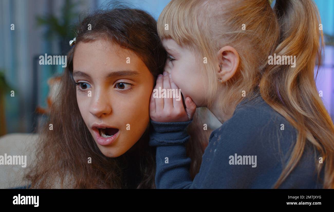 Teenage child whisper news rumors in ear to little sister kid girl ...
