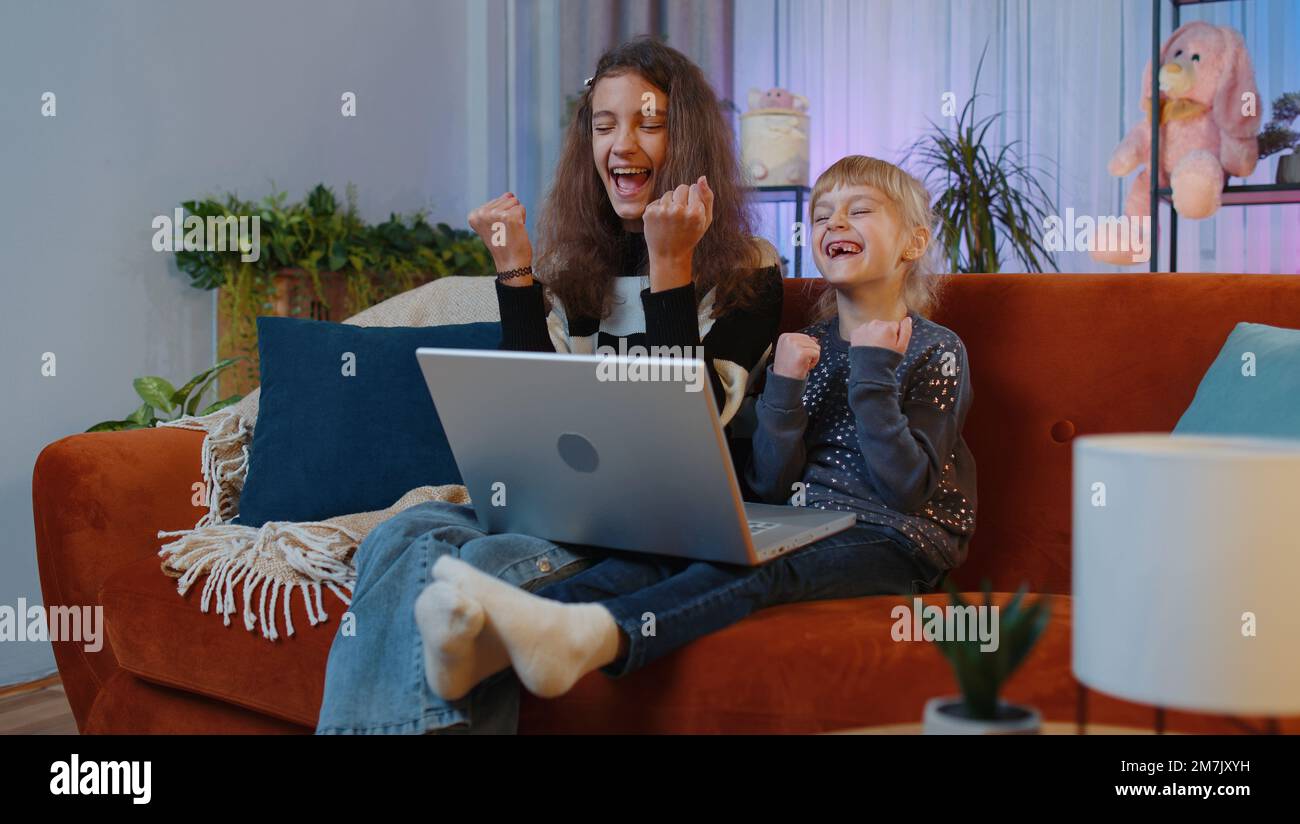 Overjoyed teenage and little sisters child kids playing on laptop raise ...