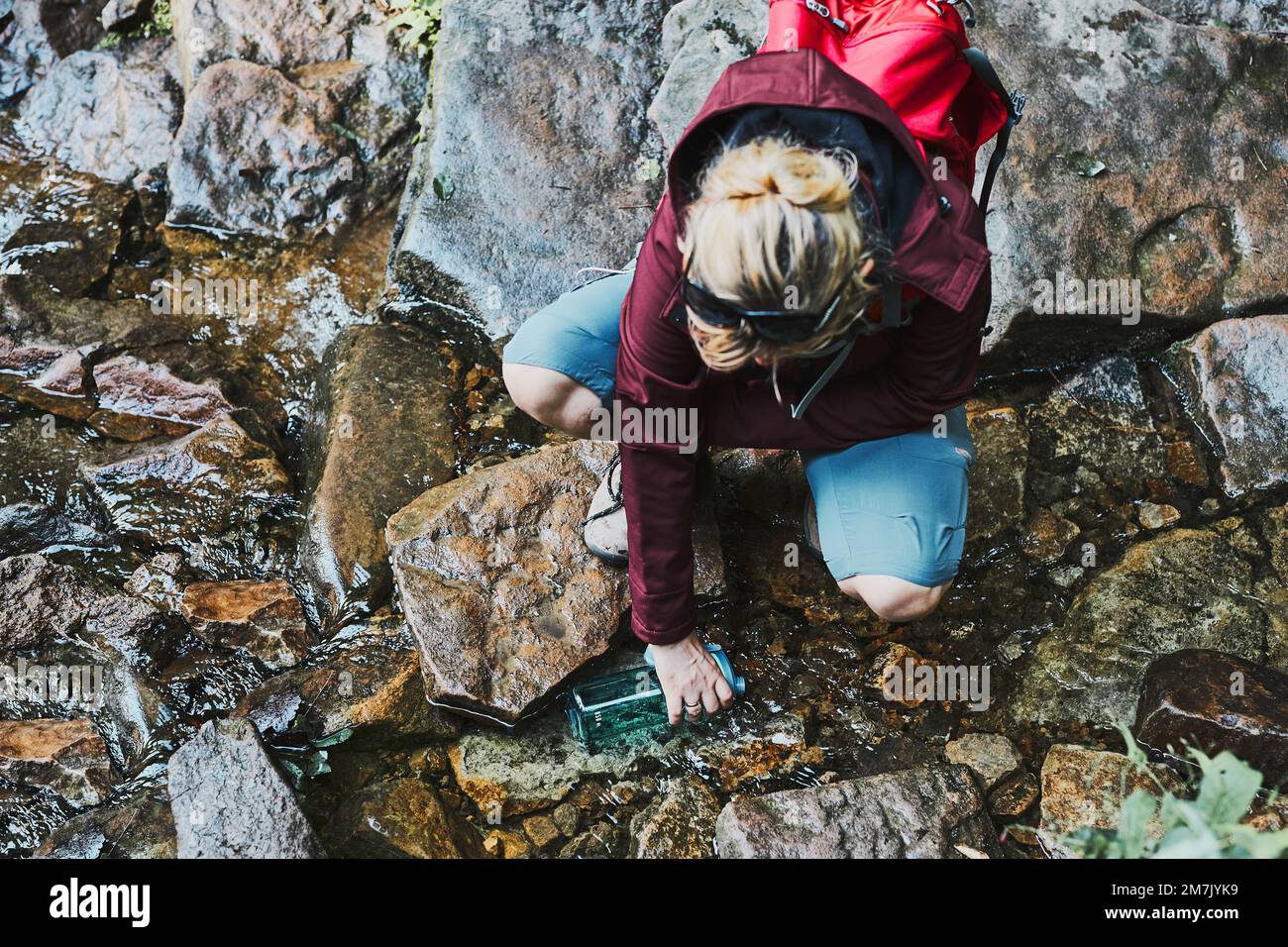 Woman taking pure water to bottle from mountain stream during trekking ...