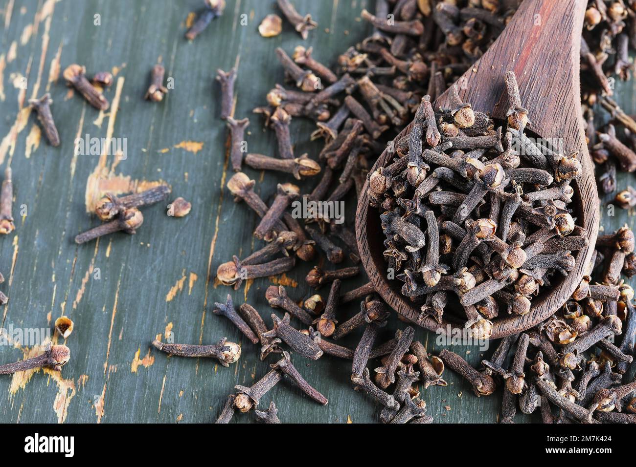 Dried cloves in a wooden spoon and scattered over a rustic wood table ...