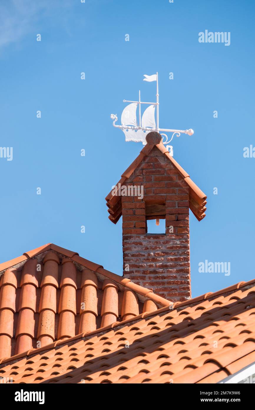 Wind vane with the shape of a sailboat over the chimney of a house in ...