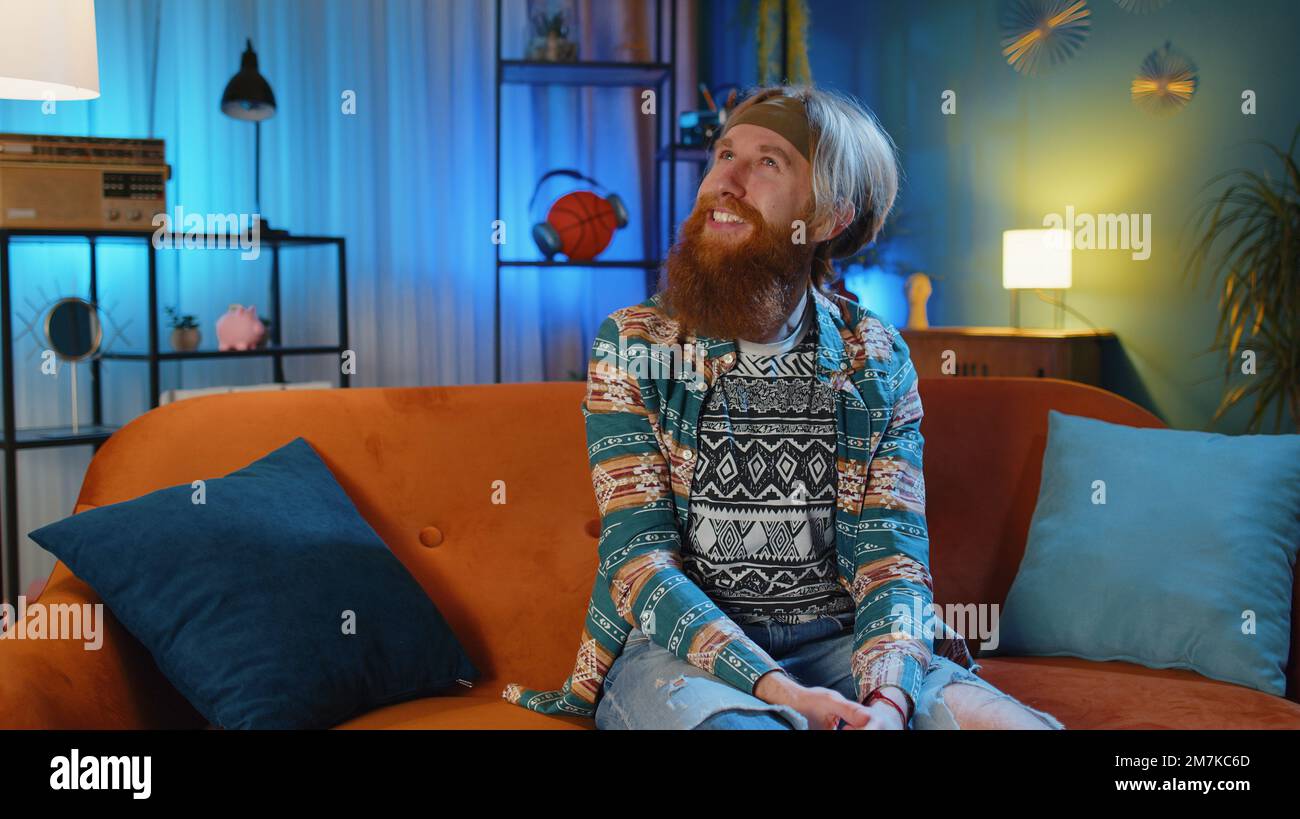 Happy calm bearded hippie redhead man at home couch smiling friendly ...