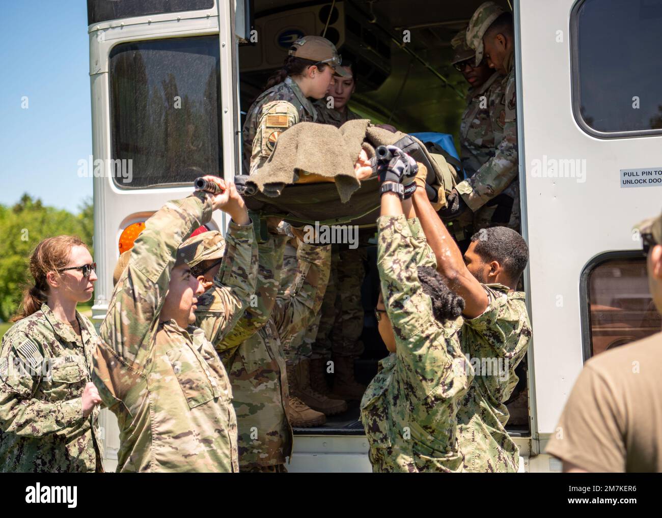 Airmen and Sailors work together to lower a gurney out of an ambulance ...