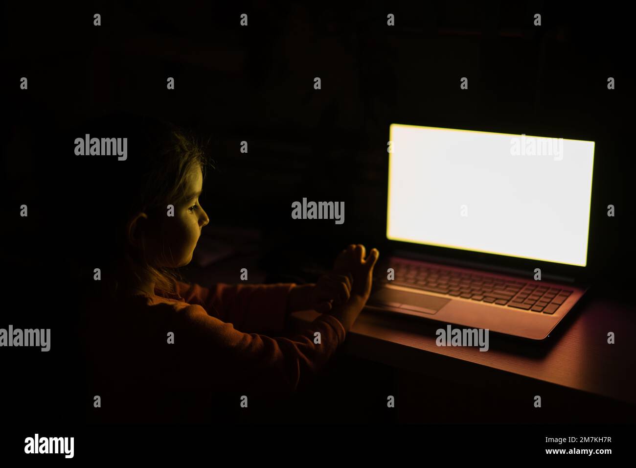 Baby girl tap on laptop while watch on colored screen in light off room ...