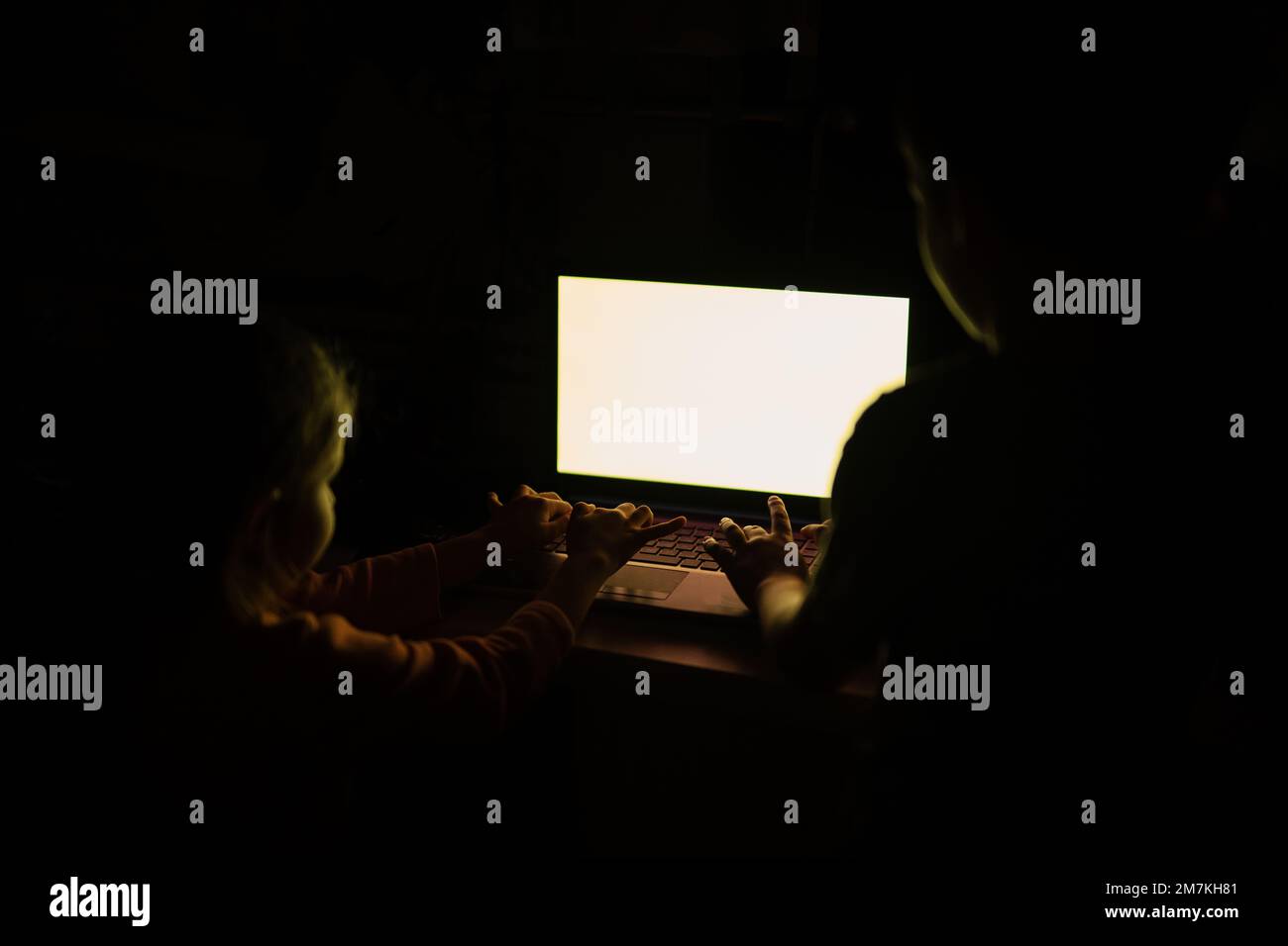 Kids tap on laptop while watch on colored screen in light off room ...
