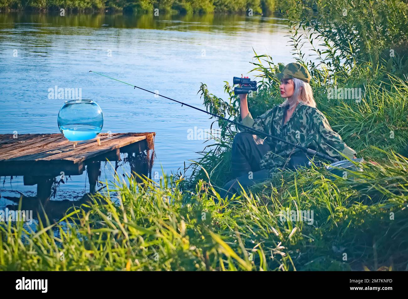 Woman fisherman carefully looks through binoculars on the river bank ...