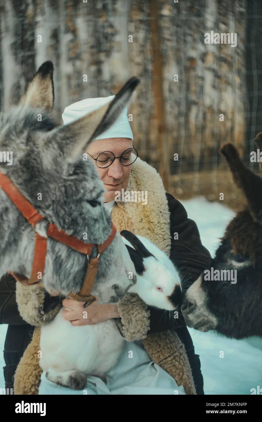 Caring doctor veterinarian holds a rabbit in his arms and a donkey next ...