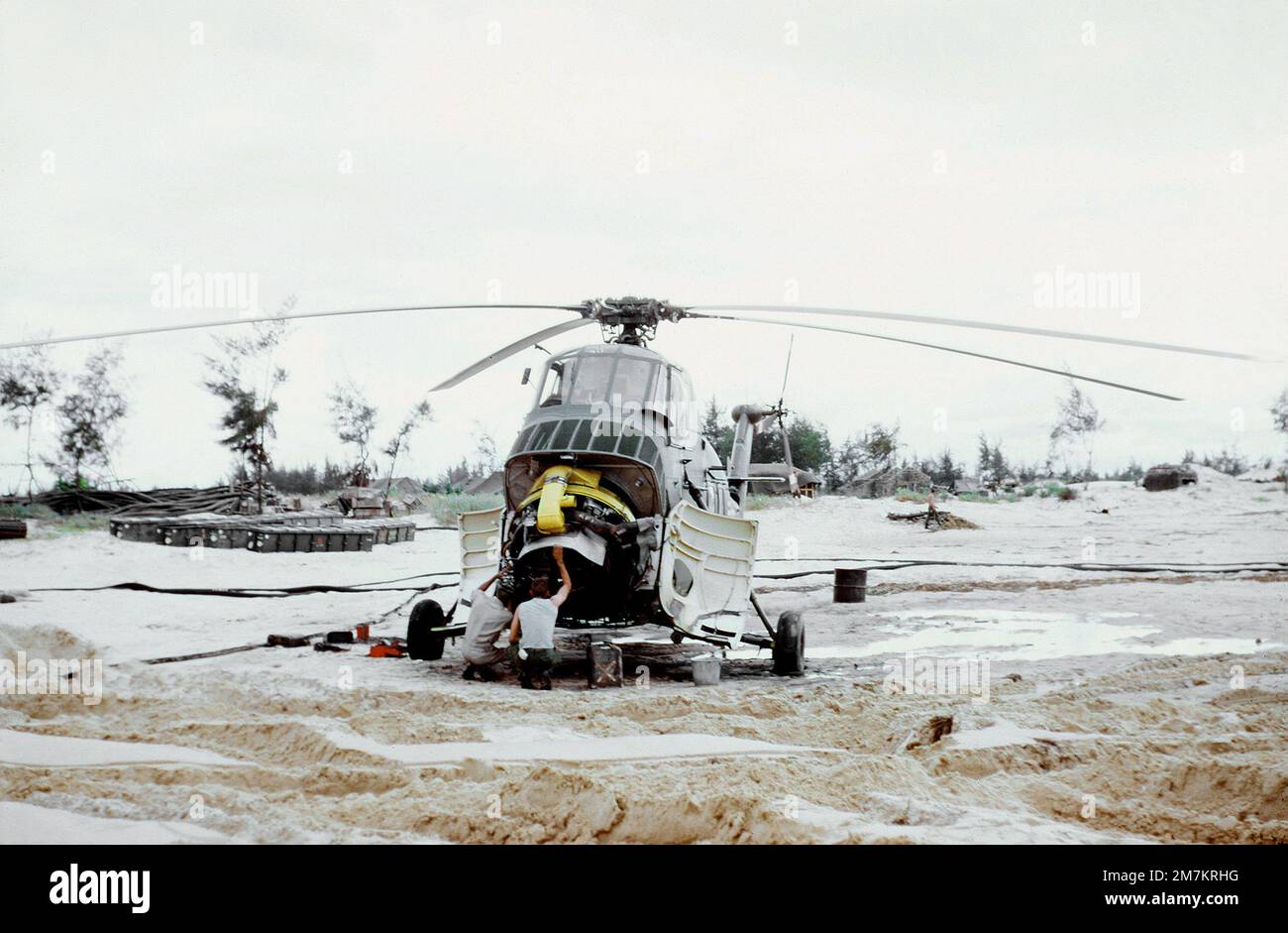 Technicians examine a disabled CH-34 Seahorse helicopter on the beach ...