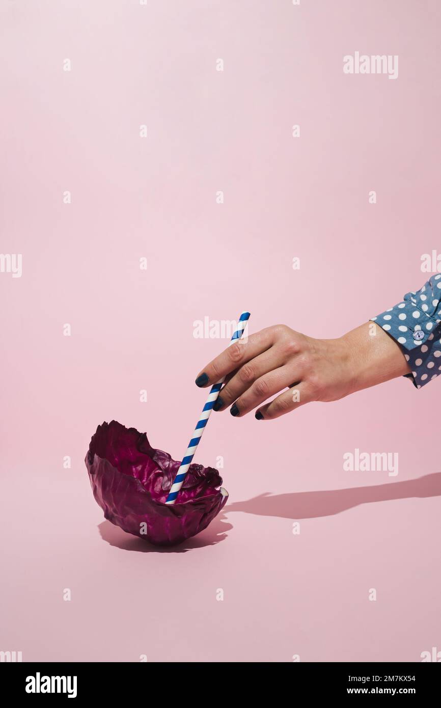 Female hand holding paper straw in leaf of red cabbage. Minimal ...