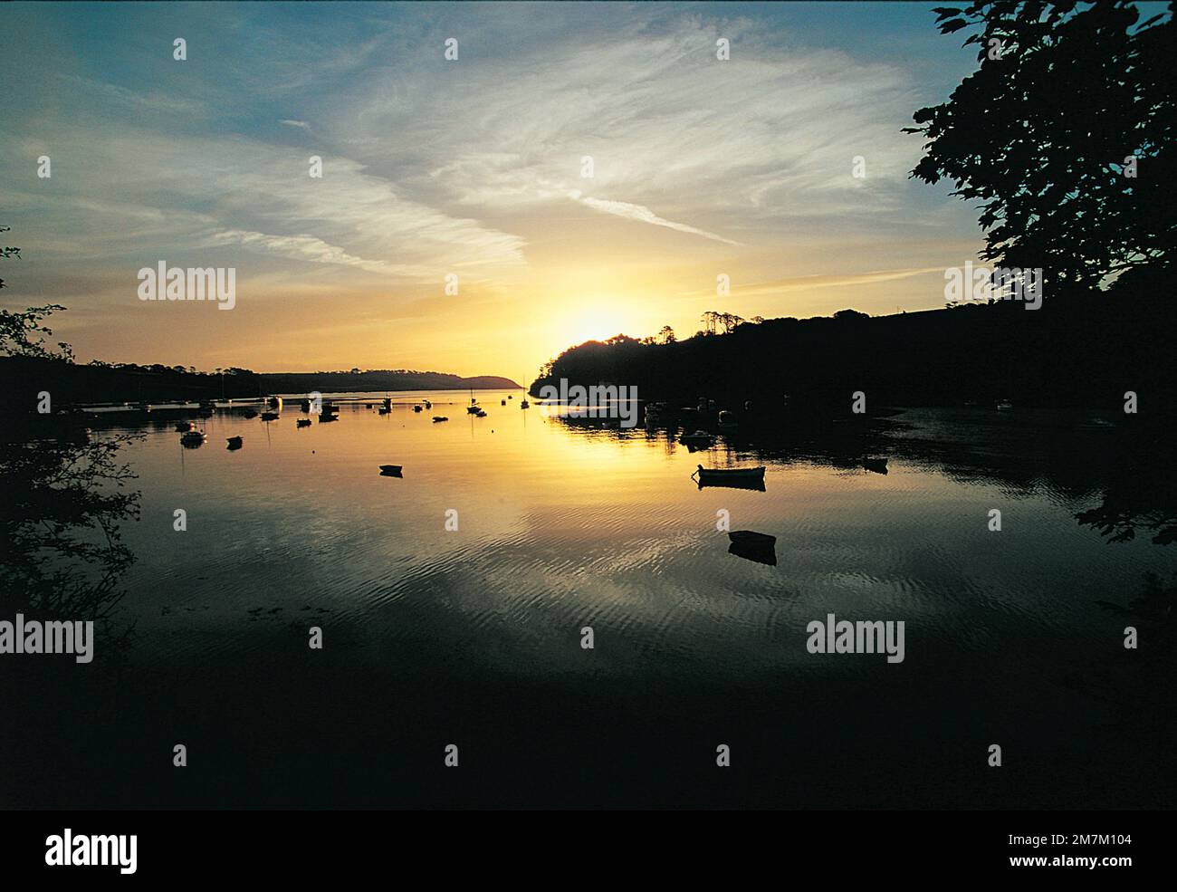 The setting sun silhouettes land on the far side of a natural harbour ...