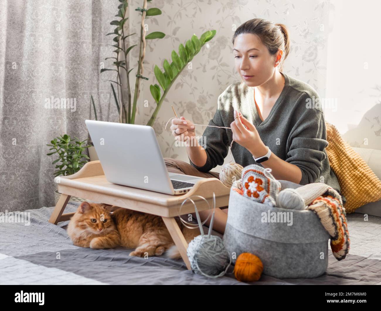 Woman is crocheting while watching movie on laptop. Learn to knit from video lessons on Internet ...
