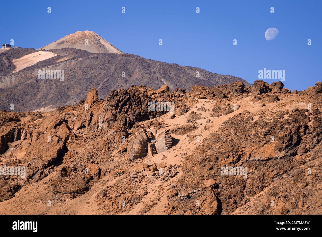 White moon in the clear blue morning sky by the peak of the volcano ...