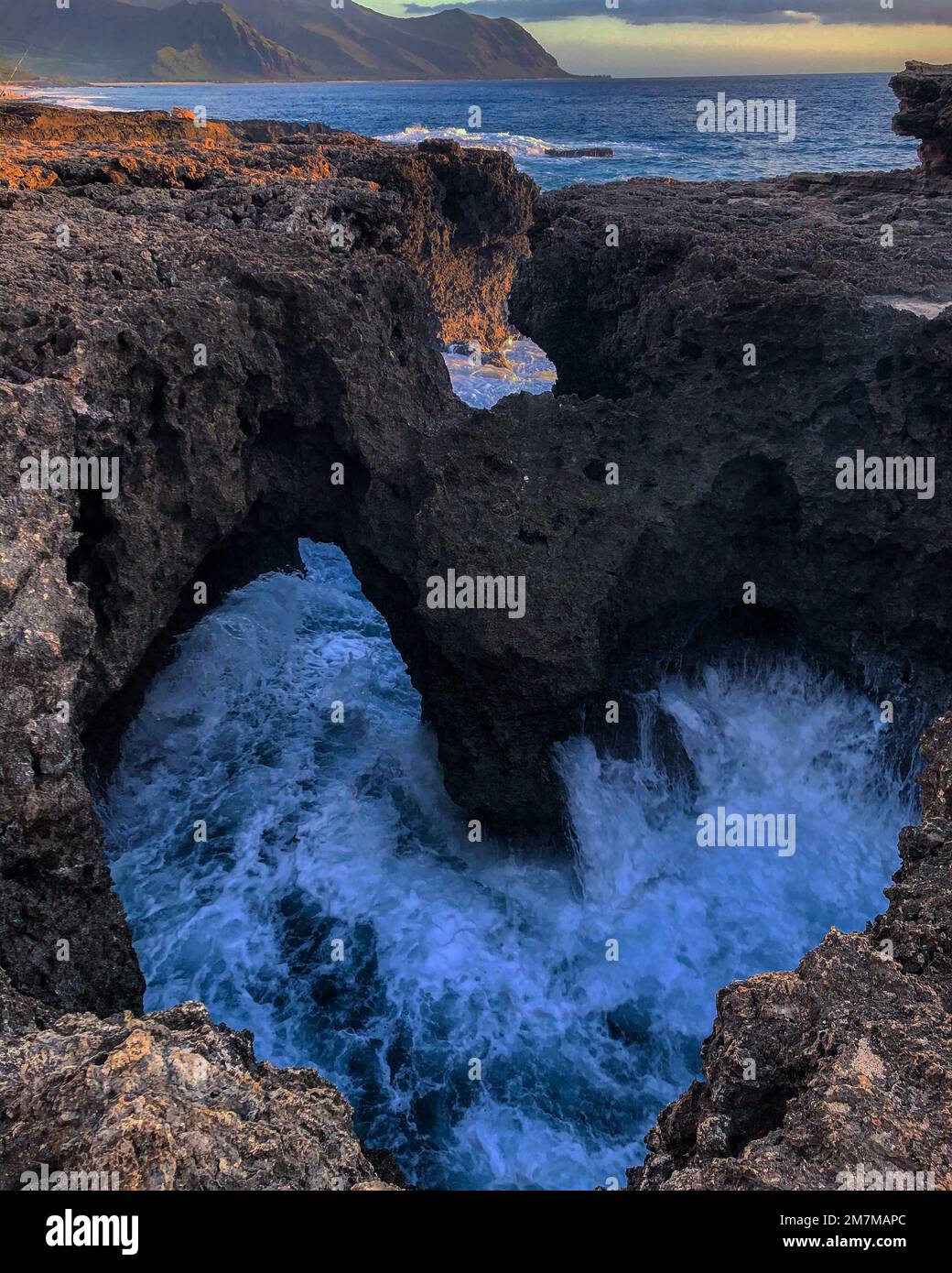 A vertical shot of the sea waves splashing at the heart shaped rocky ...