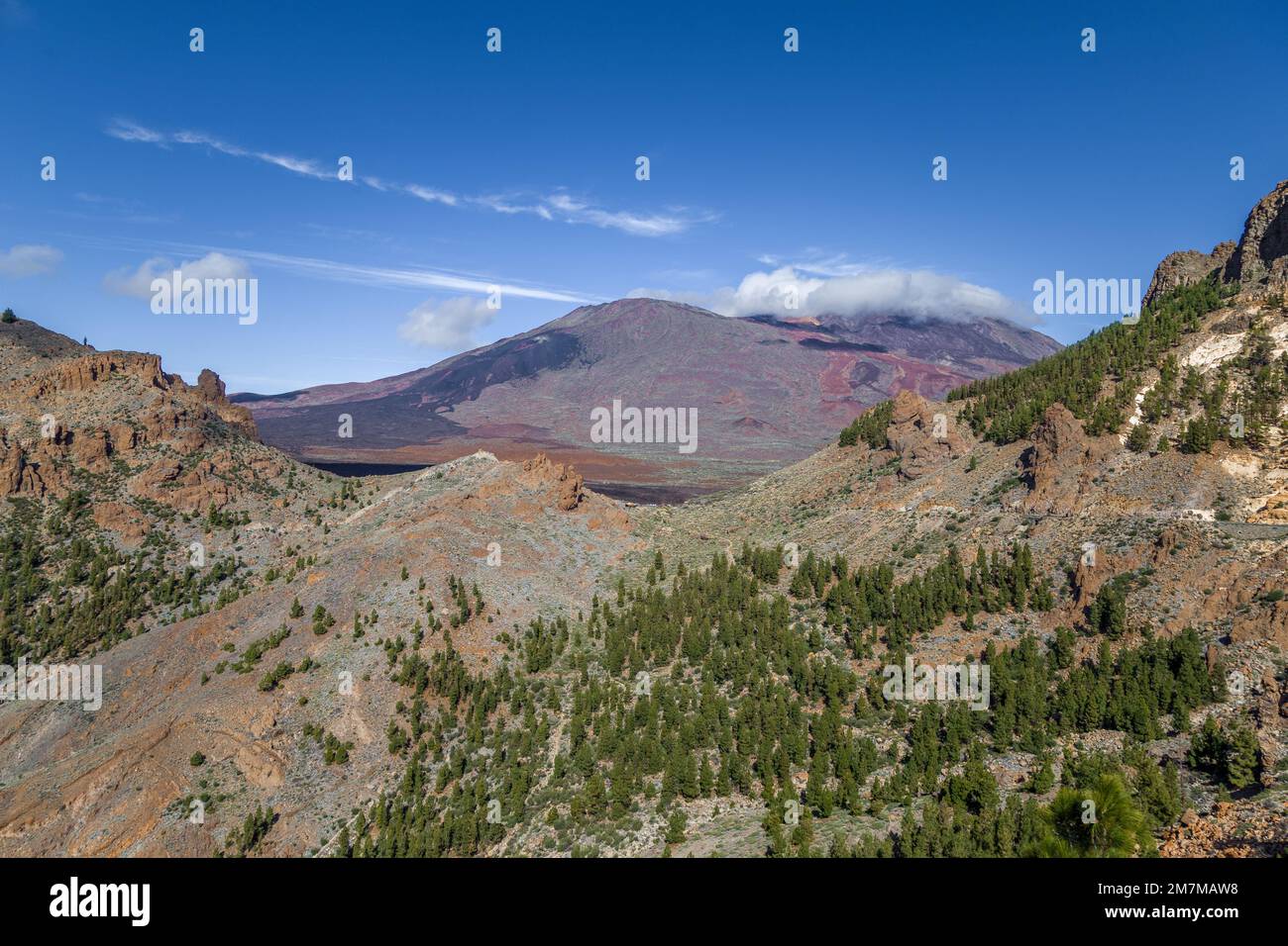 Purple tinted volcano with its peak covered by a cloud, viewed from a ...