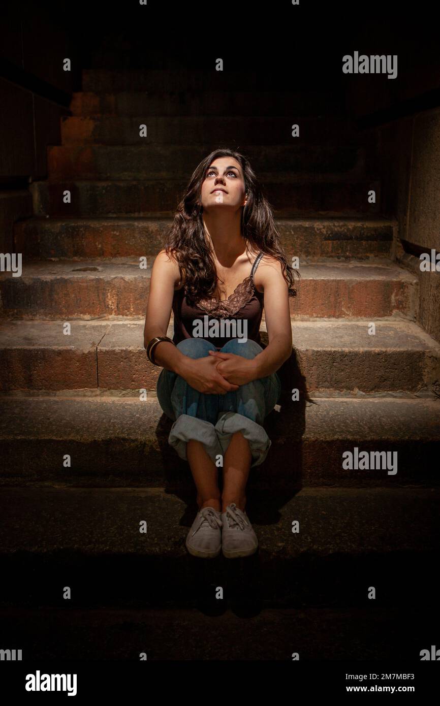 In the Dark. A vulnerable young woman sitting in a confined darkened ...