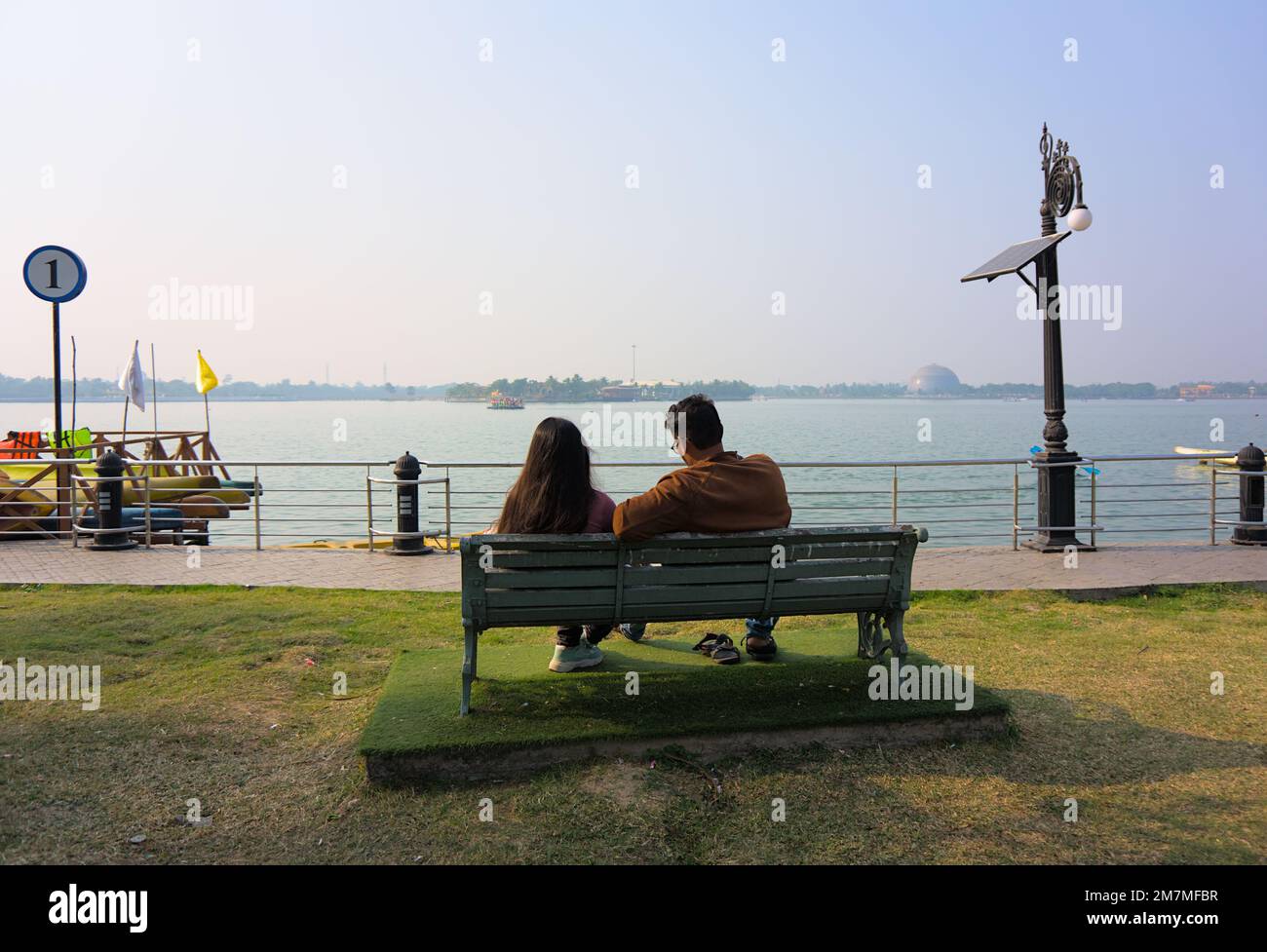 Rear View of a couple sitting on a bench facing lake. Sunny day Stock ...