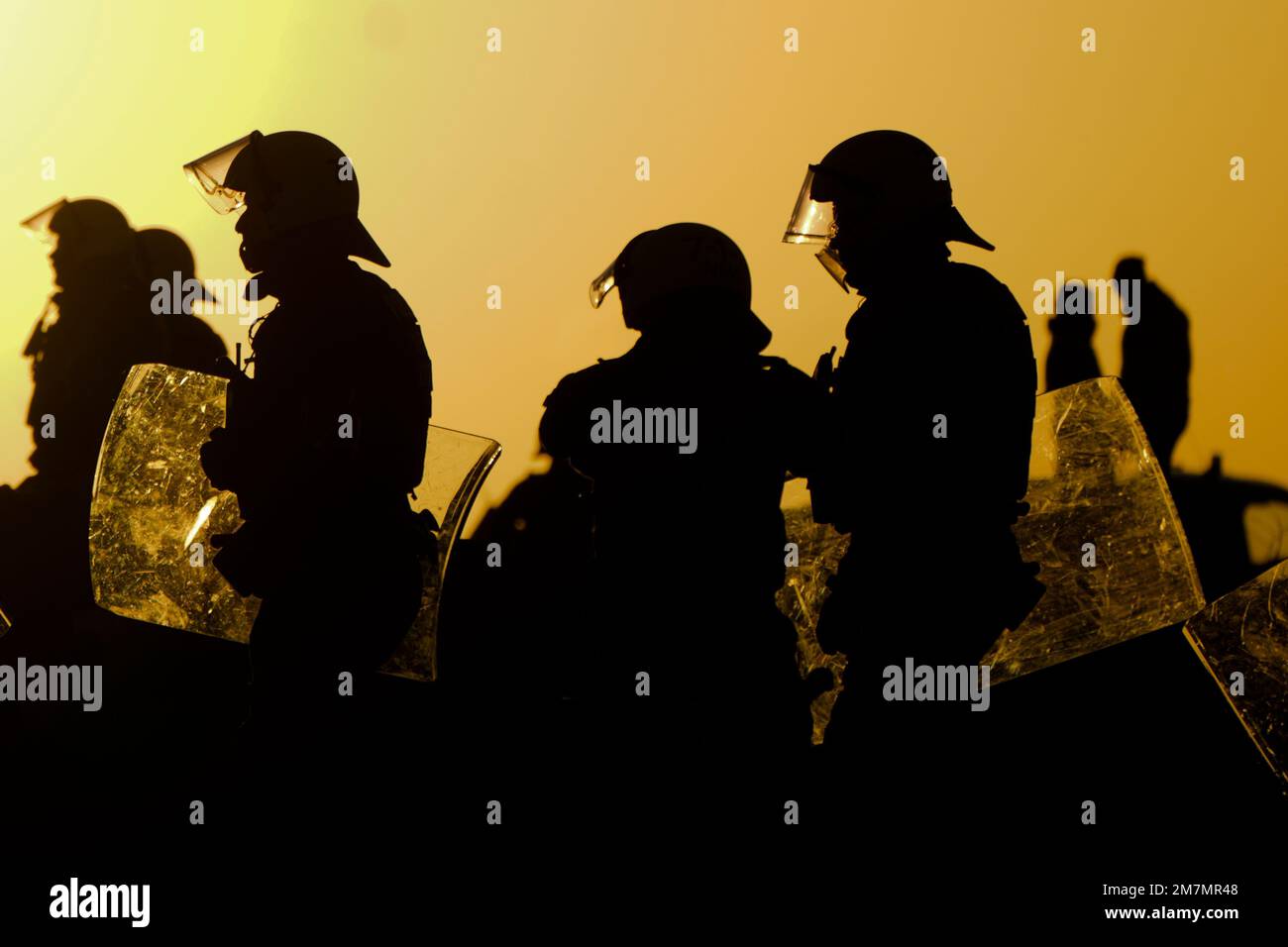 The sun rises behind police officer with riot gear at the village ...