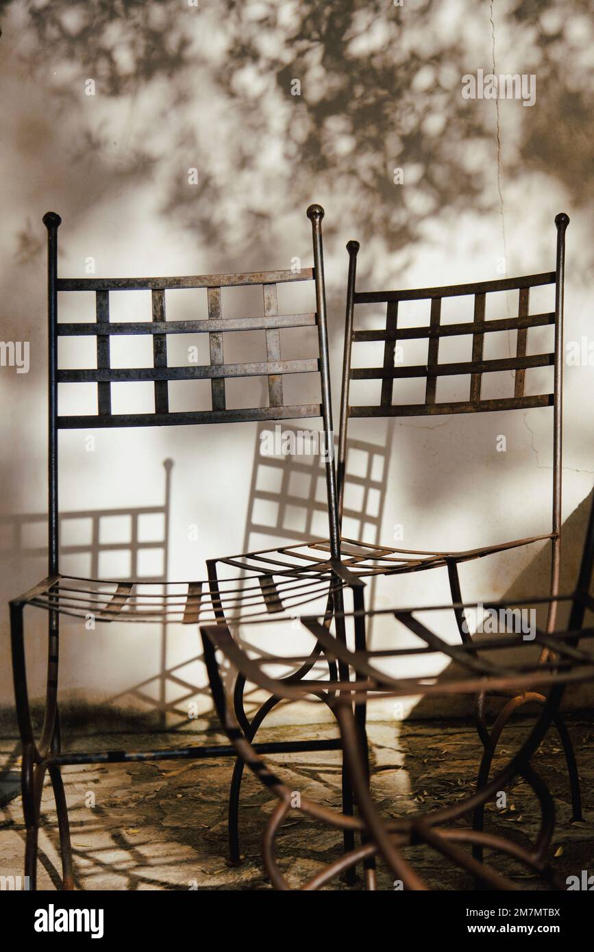 Metal chairs in the shadow play of the trees in front of a house wall ...