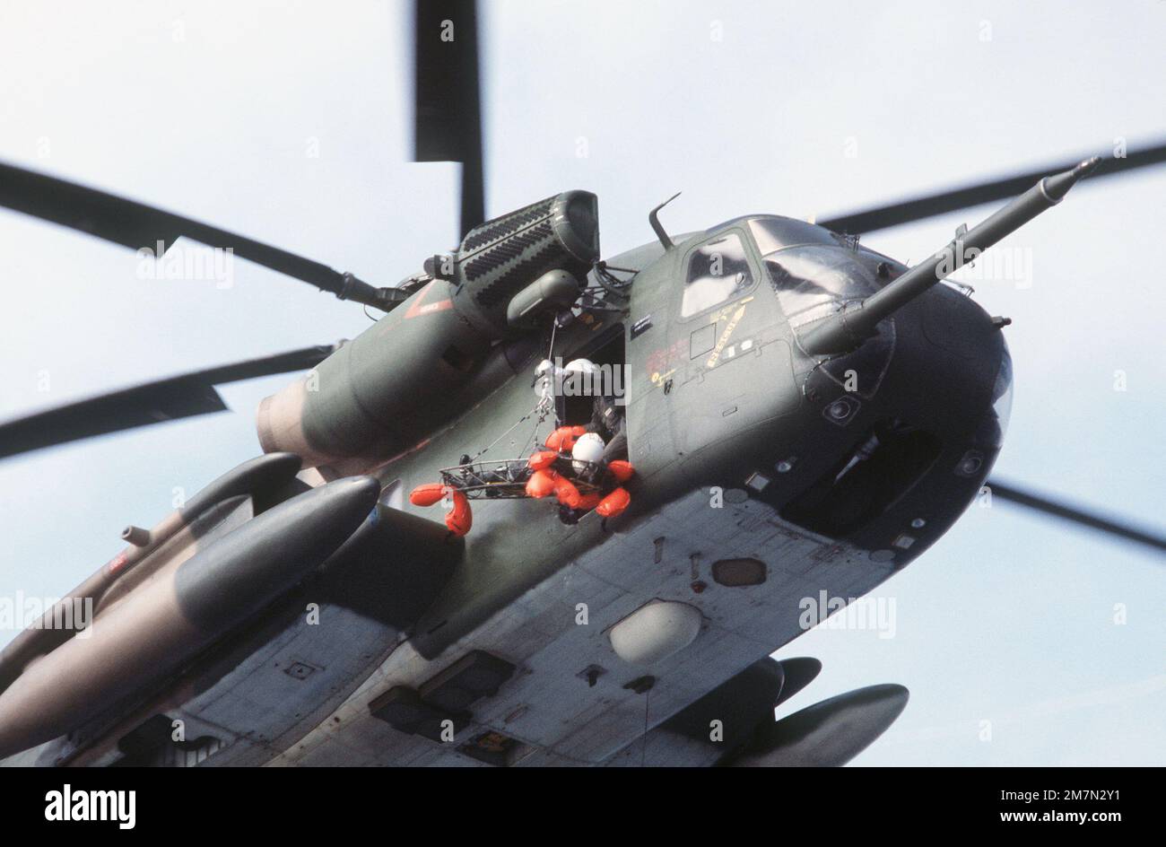 A litter carrying a "survivor" is hoisted aboard a hovering HH-53 ...