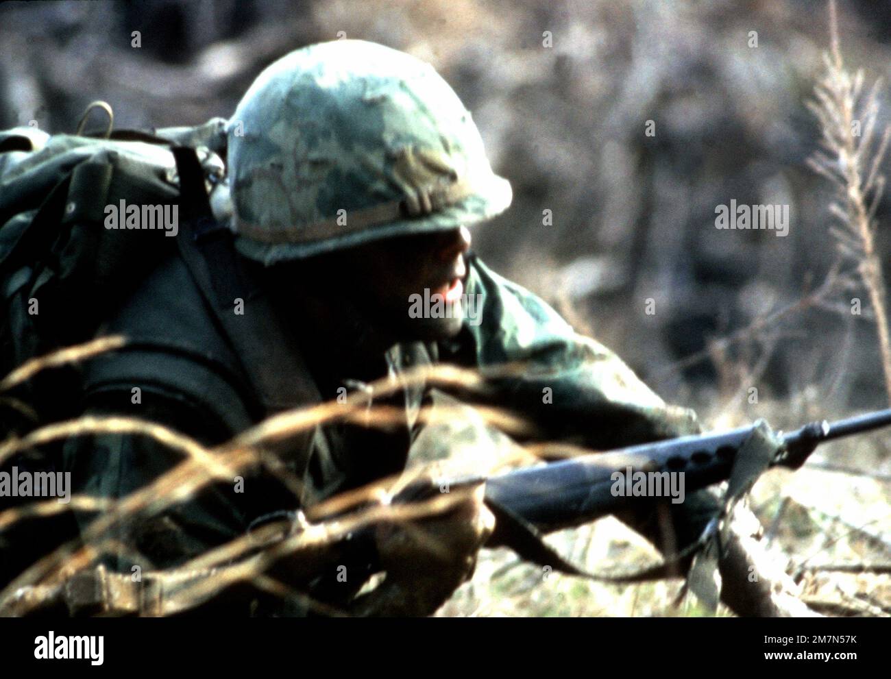 A combat-ready Marine cradles his M-16A1 rifle as he crawls through the ...