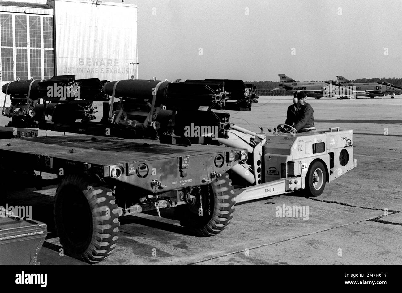 A Marine uses an ordnance carrier to unload bombs from a flat bed truck ...