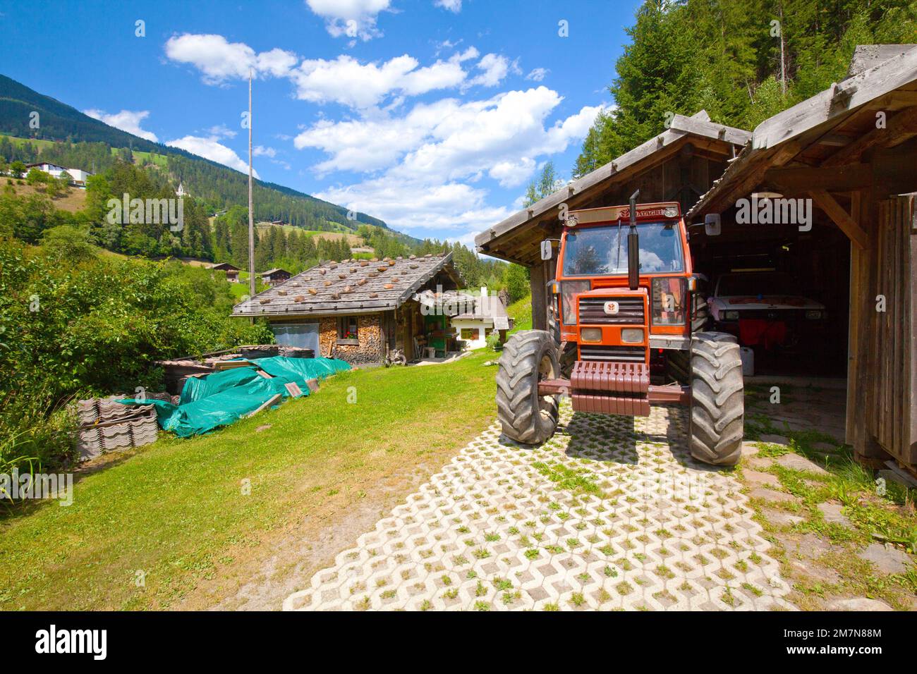 Tractor on grass pavement in front of garage, farmhouse in background ...