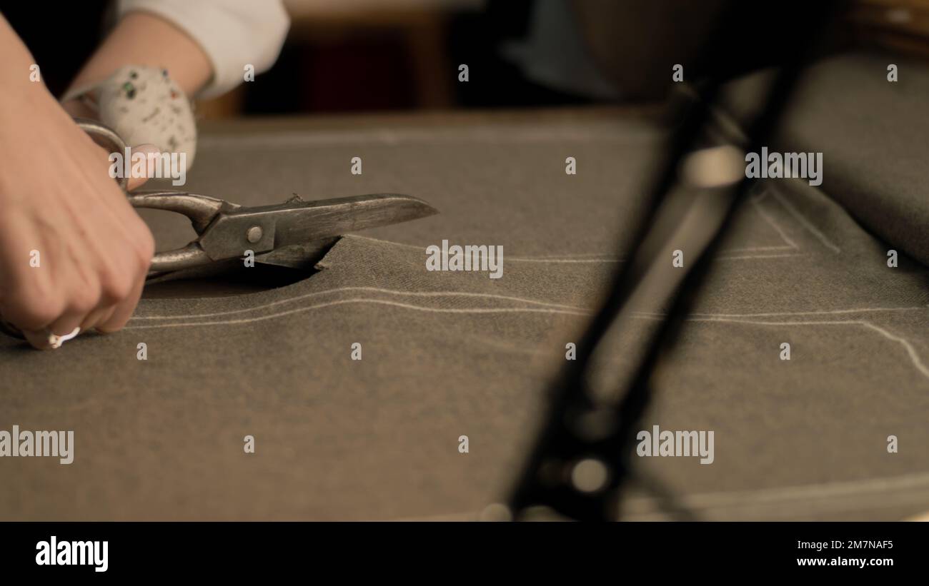 Close-up shot of female tailor cutting textile according to sketch ...