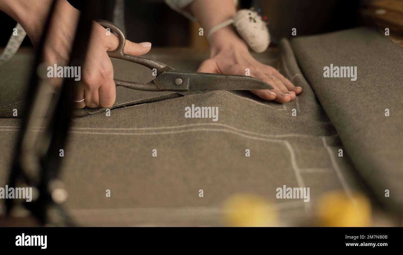 Close-up shot of female tailor cutting textile according to sketch using scissors for sewing ...