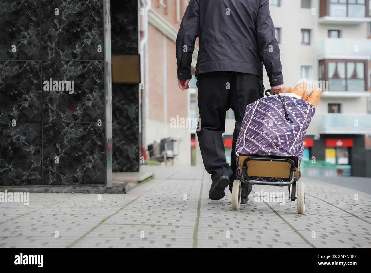 elderly man walking with a shopping cart full of bread in the street ...
