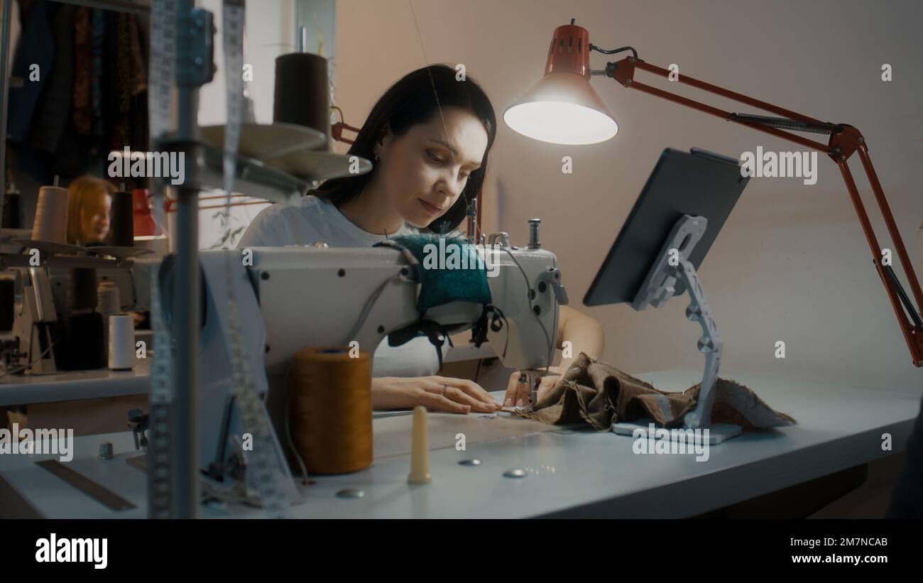 Female fashion designer or dressmaker touches tablet, sits at sewing ...