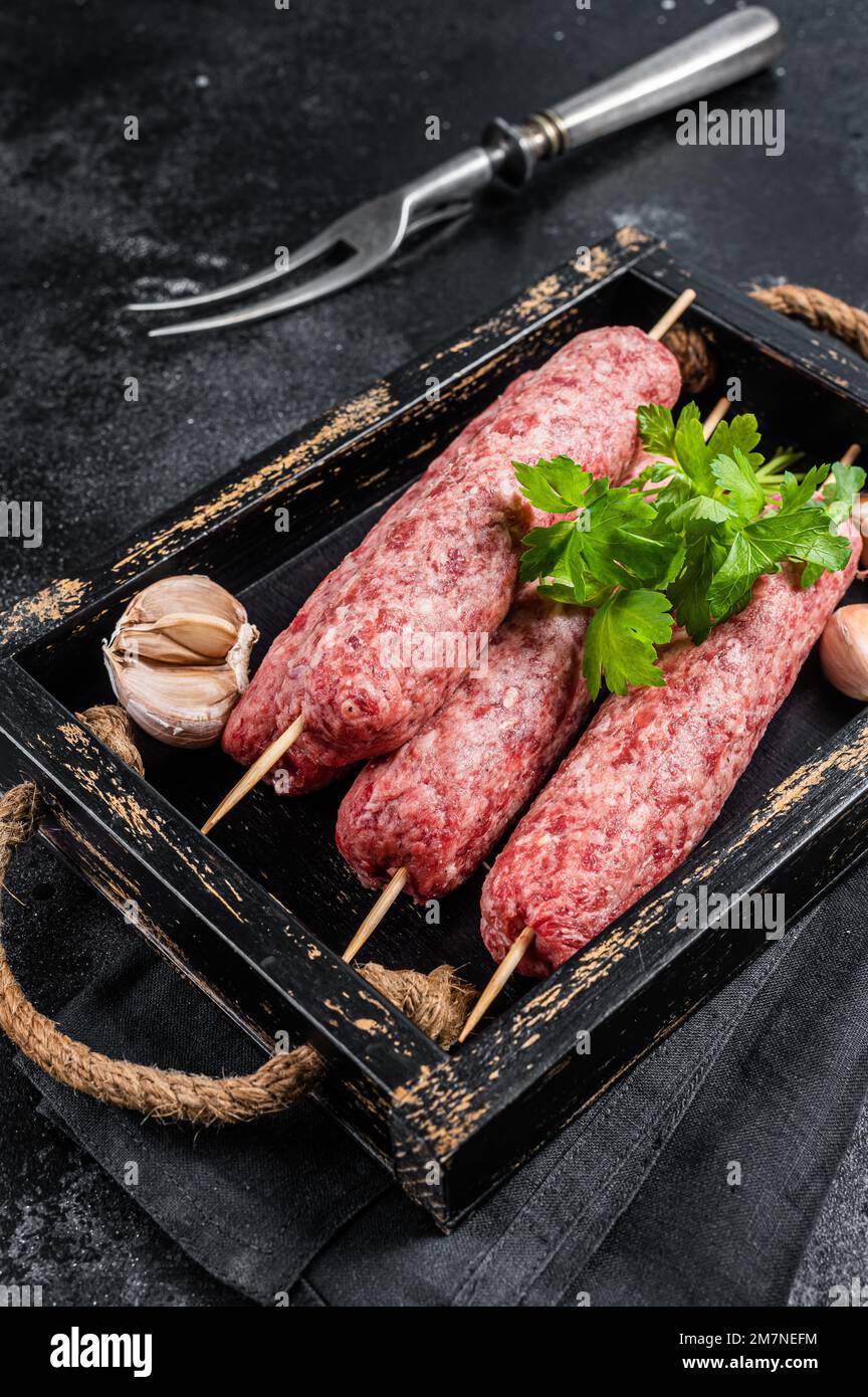 Fresh raw beef meat kebabs sausages on skewers in wooden tray. Black ...