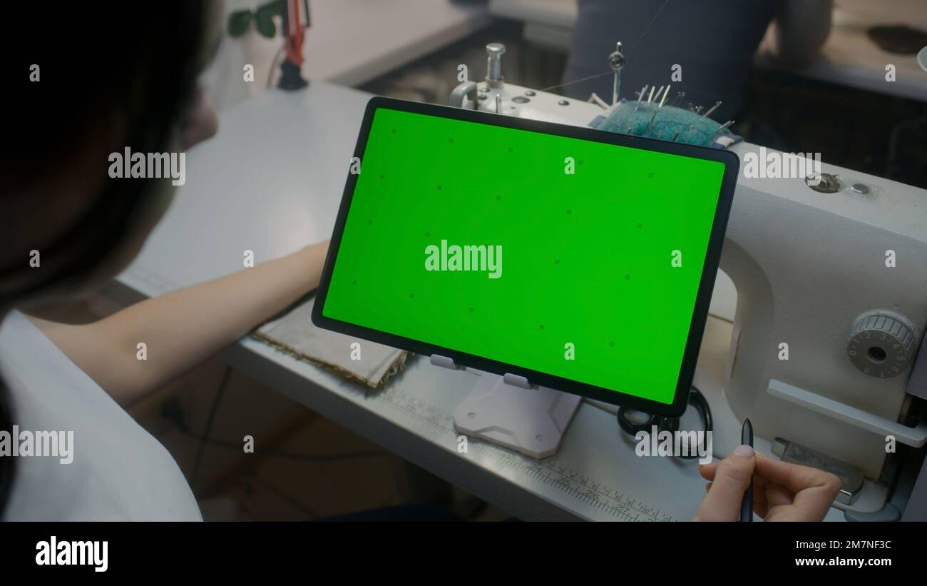 Wear designer sits at sewing machine, keeps stylus in hand, watches at ...