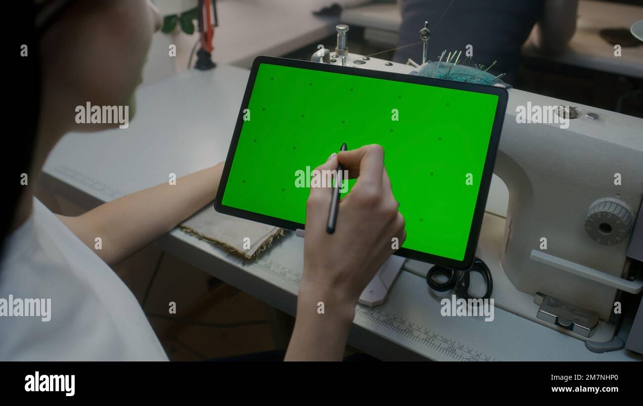 Wear designer sits at sewing machine, keeps stylus in hand, watches at ...