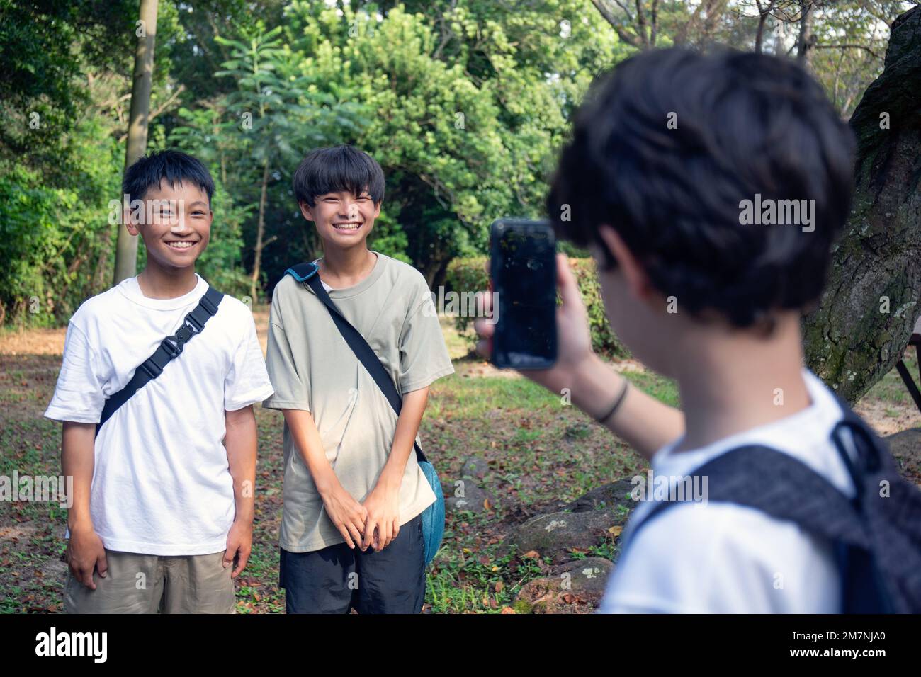 A boy with a mobile phone taking a picture of two 13 year old boys side ...